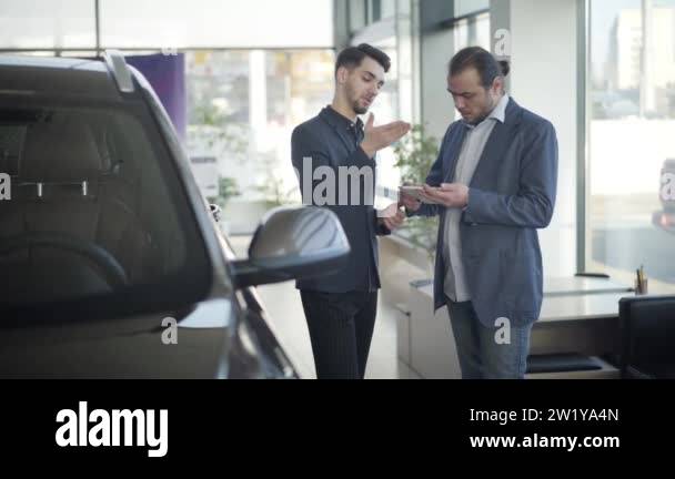 Young Caucasian car dealer giving tablet to successful rich customer in ...