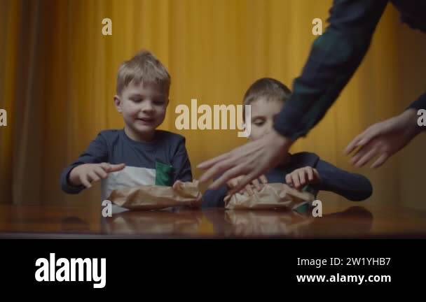 Two siblings in the same clothes eating rice chips at the table at home ...