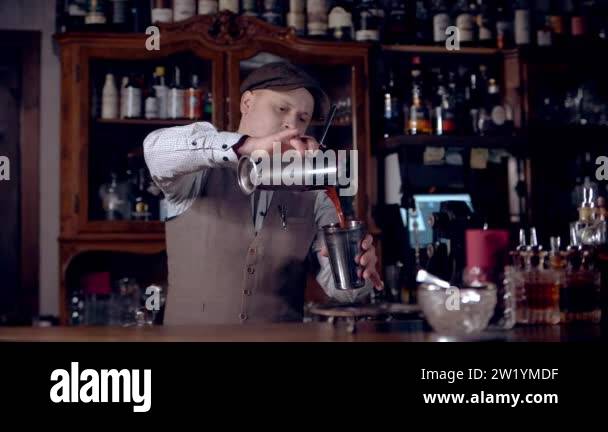 The bartender is preparing a cocktail, pouring it from a shaker into a ...