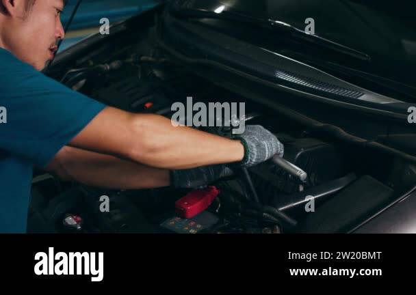 Professional car mechanic screwing details of car engine on lifted ...