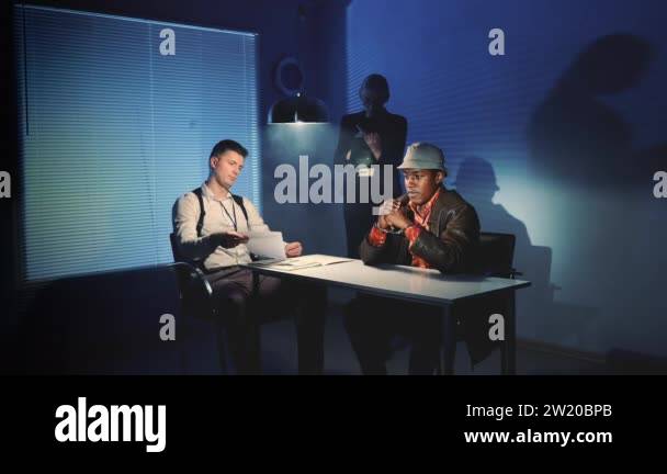Black prisoner in handcuffs having interview with caucasian detective ...
