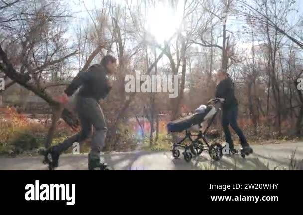 Young happy family enjoy a walk in a warm roller skating park with a ...