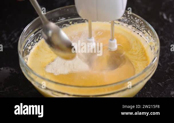 Hands mix batter in a glass bowl with mixer. Adding flour into bowl ...