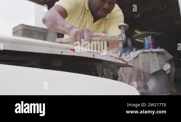 Low angle front view of an African male panel beater in a township ...