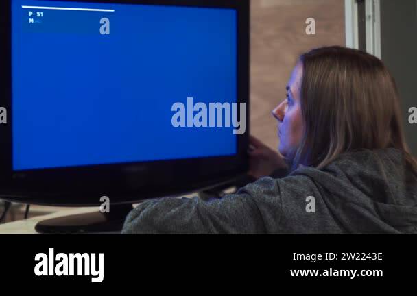 The girl looks at the blue screen, the TV monitor, switches channels ...