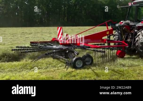 A tractor is pulling rotary rakes machinery behind it and the farmer is ...