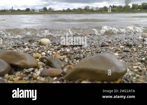 Calm flowing river water hits shore rocks at a rocky beach at a river ...