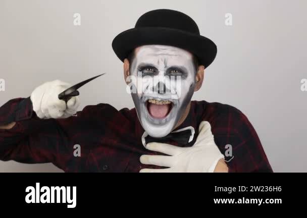 A horrible man in clown makeup threatens his victim with a sharp knife ...