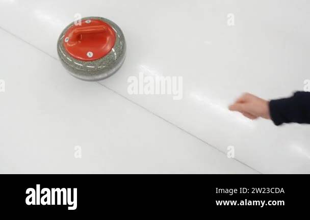 Curling game. Curler is sweeping the ice surface in the path of the ...