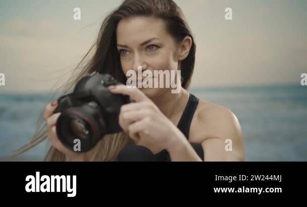 cute female photographer using her Canon camera at the beach. Sea in ...