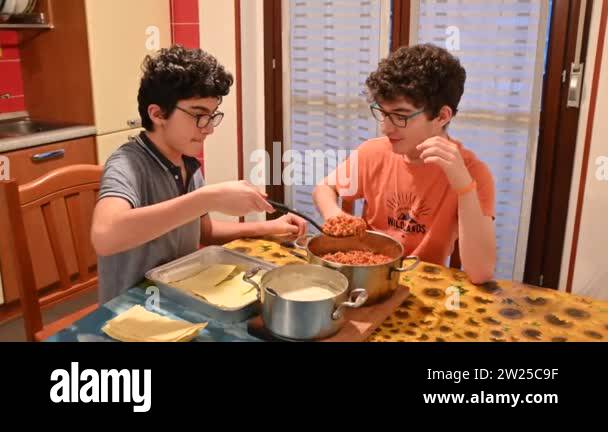 Homemade preparation of lasagna. Two Caucasian boys pour the meat sauce ...