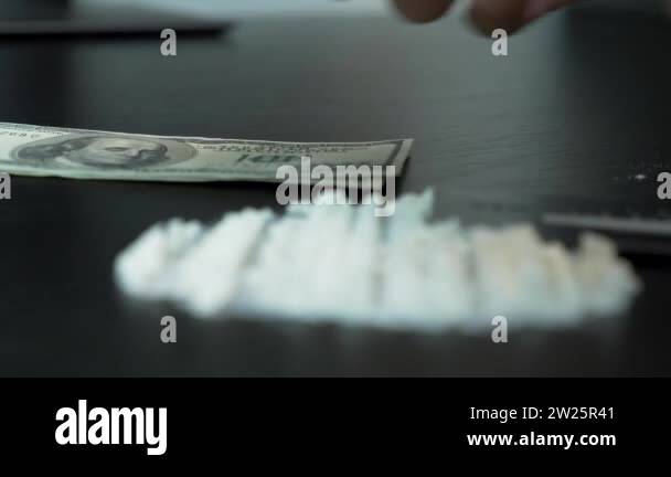 Lines of cocaine powder on black table and man is counting us dollars ...