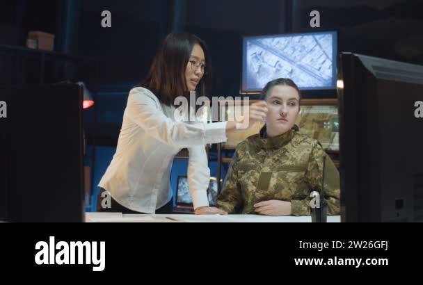 Young Caucasian girl in uniform of soldier studying in military controlling office. Asian female ...