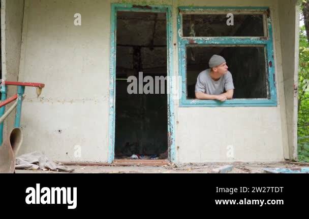 A sad homeless guy Stands on the porch of an abandoned house and looks ...