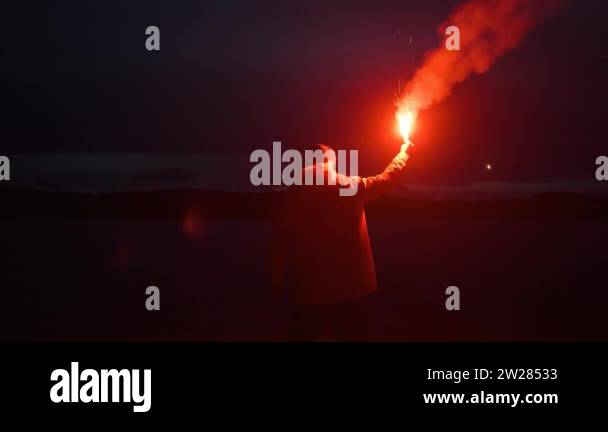 man raincoat,waving red smoke signal,light, lake mountains.traveler ...