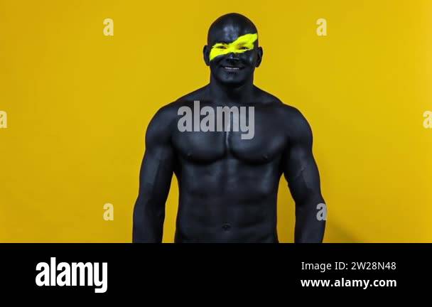 Man bodybuilder athlete with yellow color on face art and black body ...