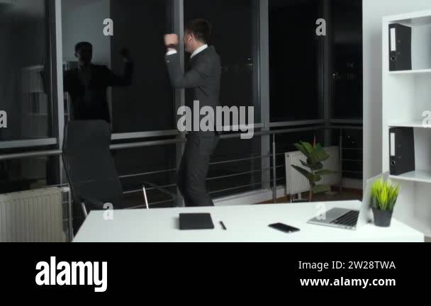 Happy male businessman dancing in his office by the panoramic window ...