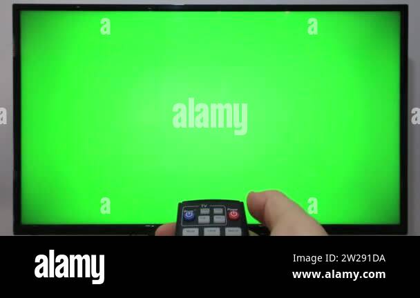 Person pointing a TV remote and pressing buttons in front of a TV with ...