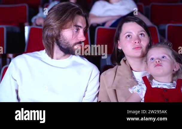 Friendly family watching a movie in the cinema. Media. Young parents ...