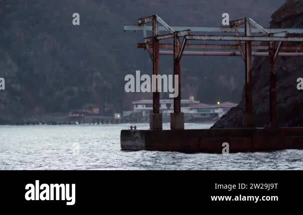 Rusty pier on rocky coast. Shot. Old ships wharf is empty on background ...