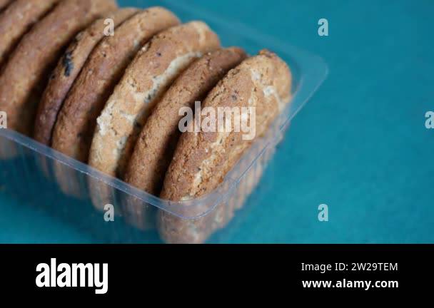 Oatmeal cookies lie in transparent open plastic tray. Male hand takes ...