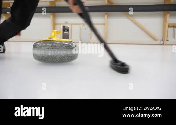 Curling game. Curler is sweeping the ice surface in the path of the ...