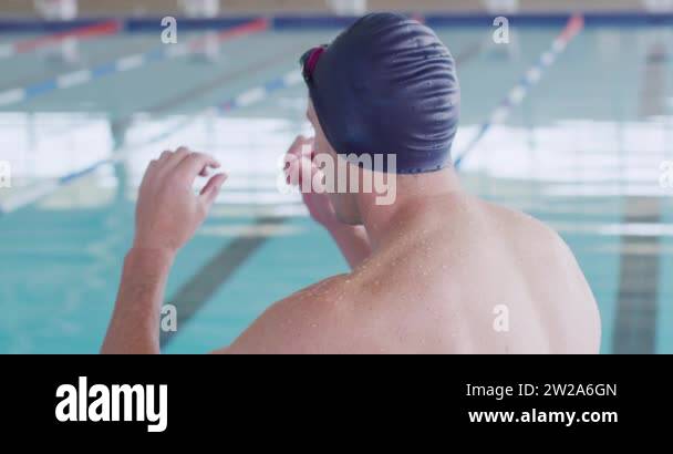 Rear view of Caucasian male swimmer at swimming pool, putting on his ...
