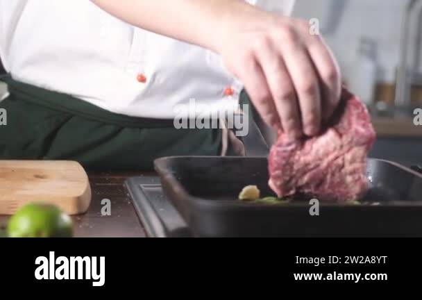 chef puts fresh piece of beef meat in frying pan in kitchen of ...