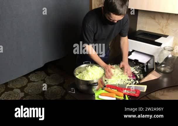 A man wearing a medical mask puts chopped cabbage into a saucepan ...