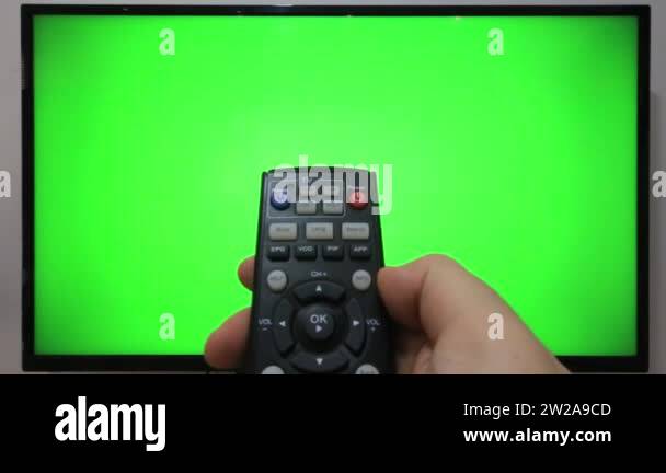 Person pointing a TV remote and pressing buttons in front of a TV with ...