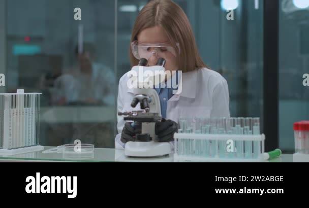 microbiologist woman is exploring sample in laboratory, looking into microscope, specialist of ...