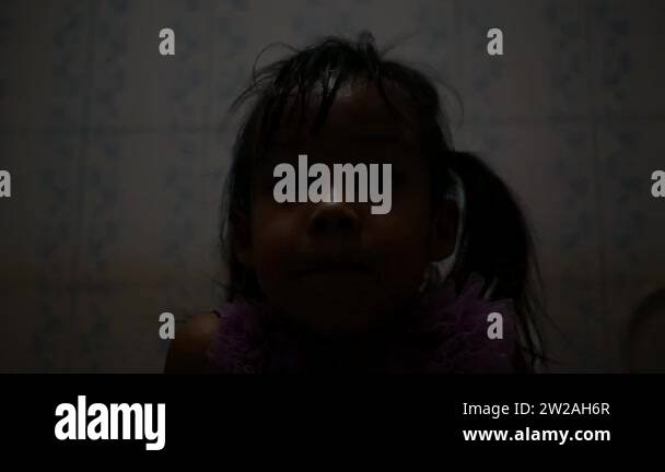 Cute little girl feel scared while sitting on the toilet bowl with broken flickering fluorescent ...