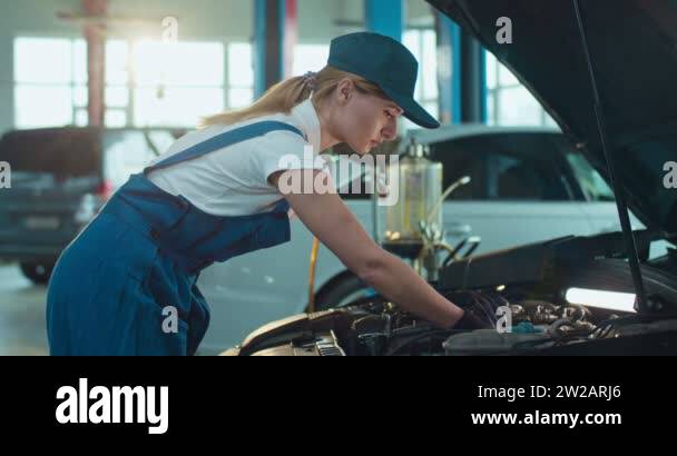 Female Caucasian young auto mechanic standing at open car and repairing ...