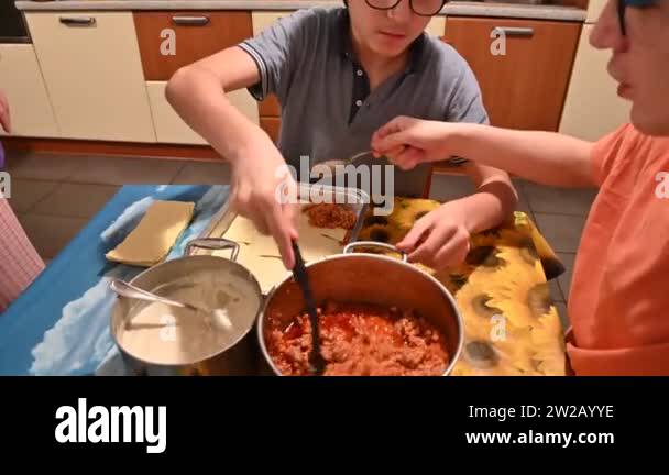 Homemade preparation of lasagna. Two Caucasian boys help their mother ...