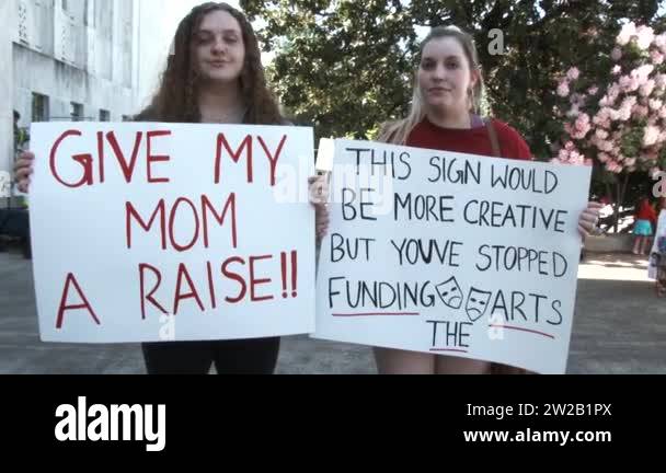 Two students holding signs standing up for better teacher wages and ...