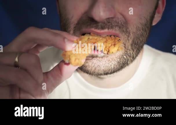 Close-up, a man with stubble eating a chicken leg. Holds nuggets with ...
