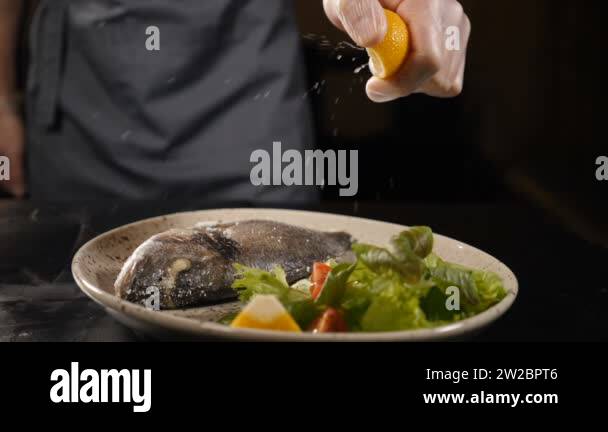 Slow motion food footage of chef squeezing a half cut lemon over fish ...