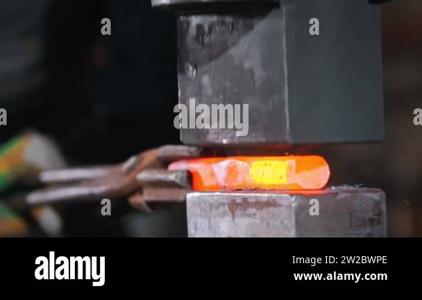 Blacksmith putting a longer piece of incandescent metal under the pressure of industrial forging ...
