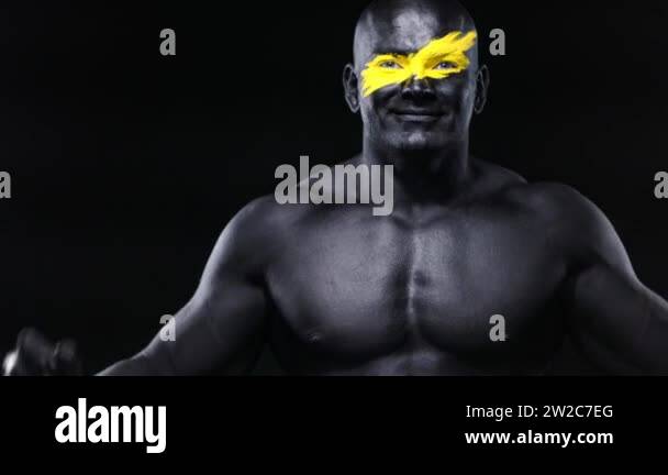 Man bodybuilder athlete with yellow color on face art and black body ...