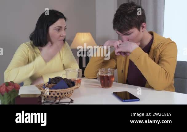 Upset teenage Caucasian boy closing face with hands as his angry mother ...