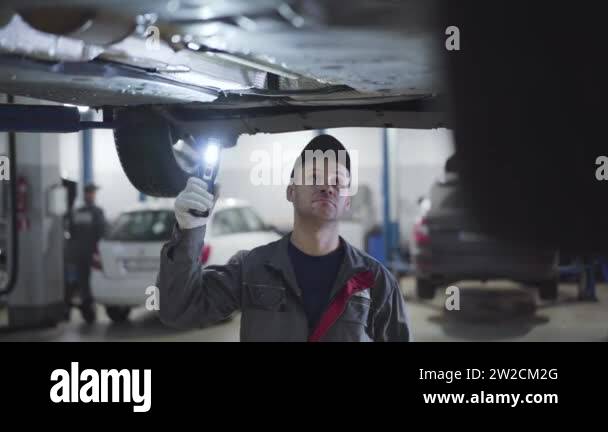 Serious Caucasian man in workwear and cap walking under car bottom with ...