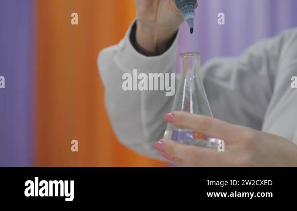 Drop of dye from the pipette falls into a flask of clear water ...