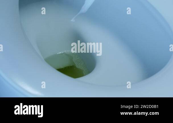 Male hand flushes urine in white toilet bowl, close up. Side view of ...