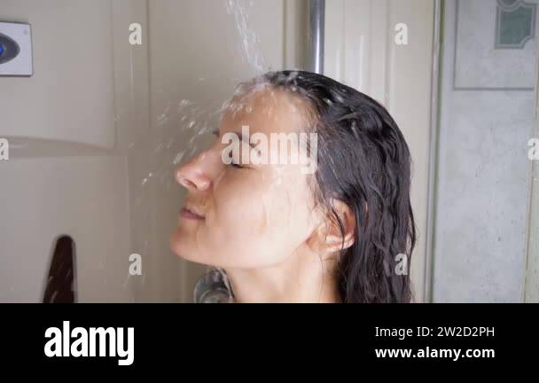 Young woman takes a shower while standing under stream of water. Girl ...
