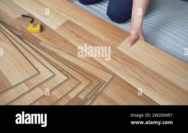Man installing laminated floor tiles over white foam base layer, detail ...