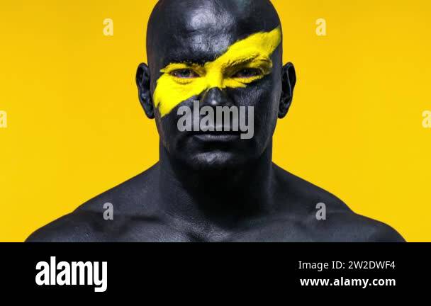 Man bodybuilder athlete with yellow color on face art and black body ...