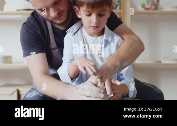 Close up of man and his son are making pot from clay on throwing wheel ...