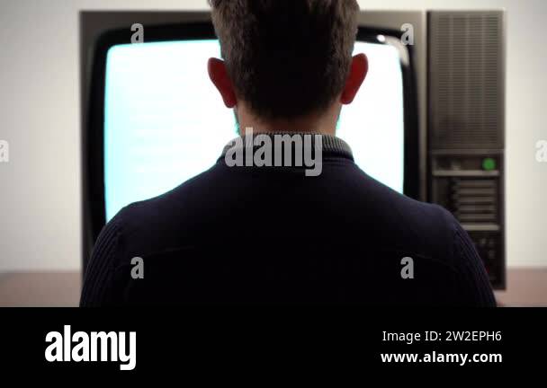 Back view of male sitting in front of vintage TV screen with noise ...