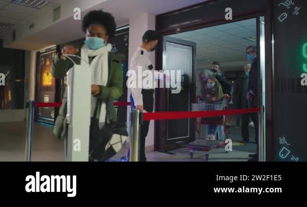 Diverse crowd walking past guard with thermometer and disinfecting ...