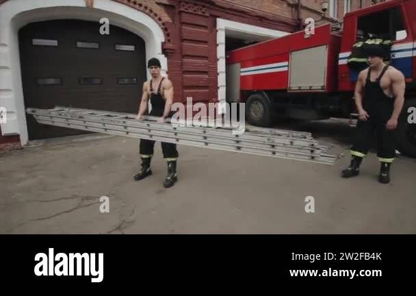 Two muscular young men are training near their fire engine. Jump and ...